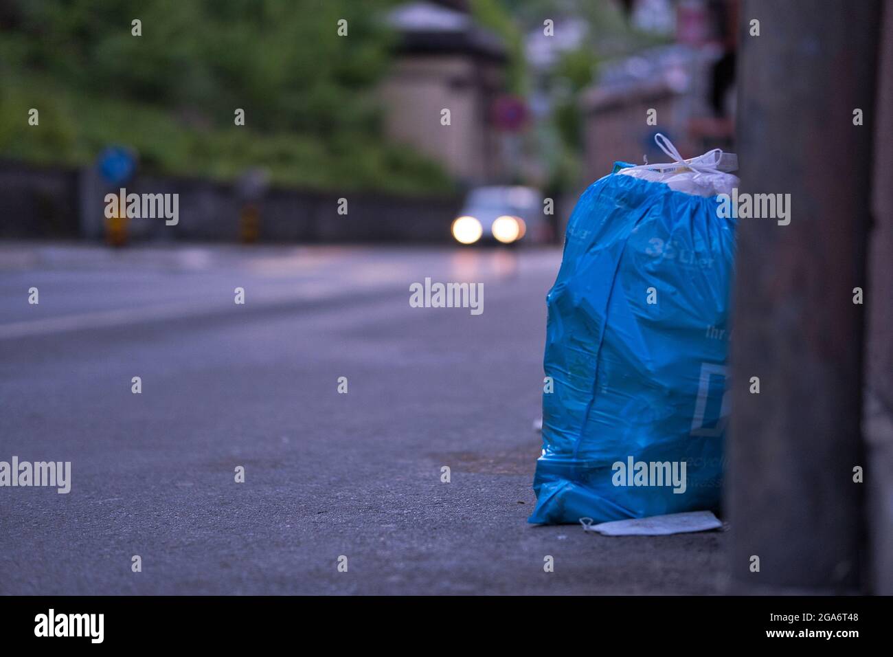 Shallow focus of a blue closed sack standing next to wall in the street ...