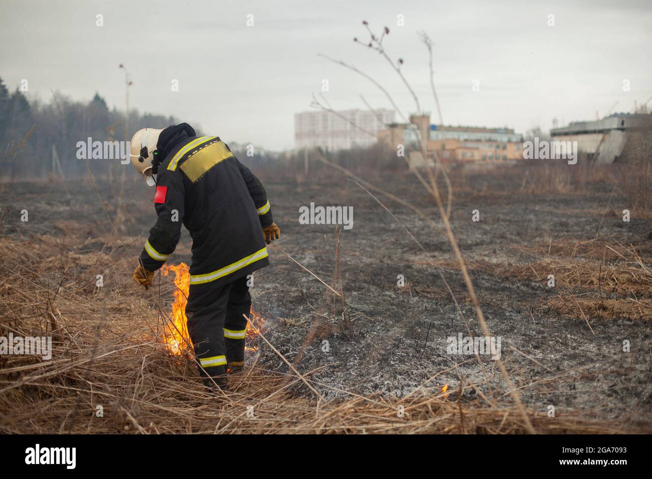A firefighter extinguishes dry grass. A firefighter is fighting a fire ...