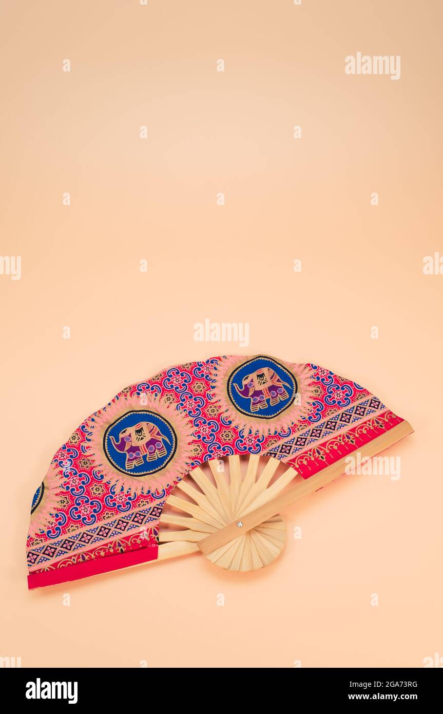 Vertical shot of an artistic hand fan isolated on a coral background ...