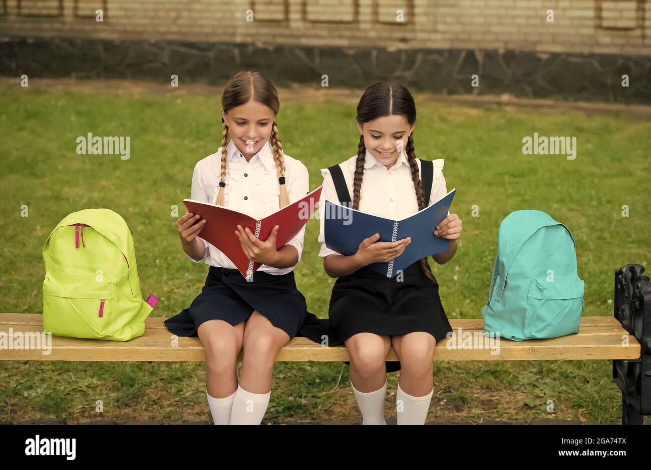 Little kids in school uniforms read library books sitting on bench ...