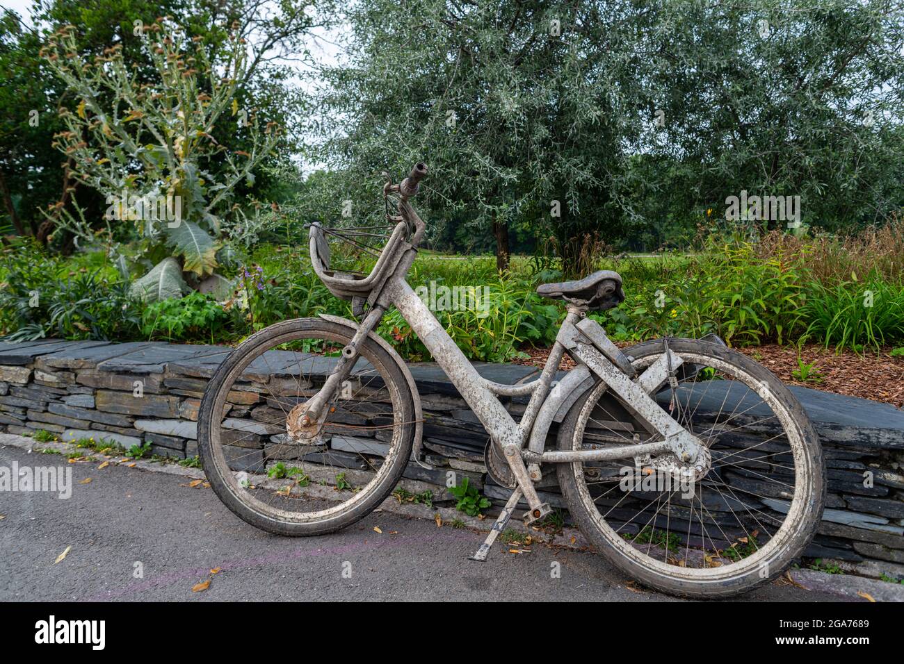 an abandoned bike totally dirty and rusted on a small wall in a park ...