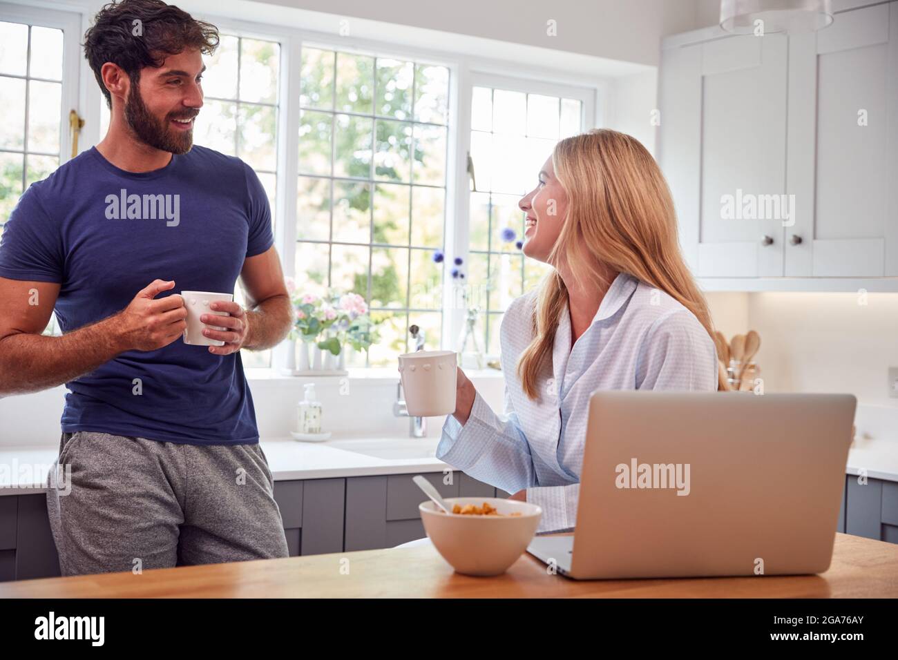 Couple Wearing Pyjamas In Kitchen With Laptop Eating Breakfast Together ...
