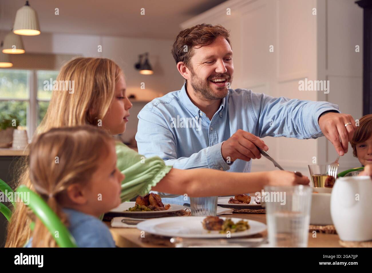 Family Sitting Around Table At Home Enjoying Meal Together Stock Photo ...