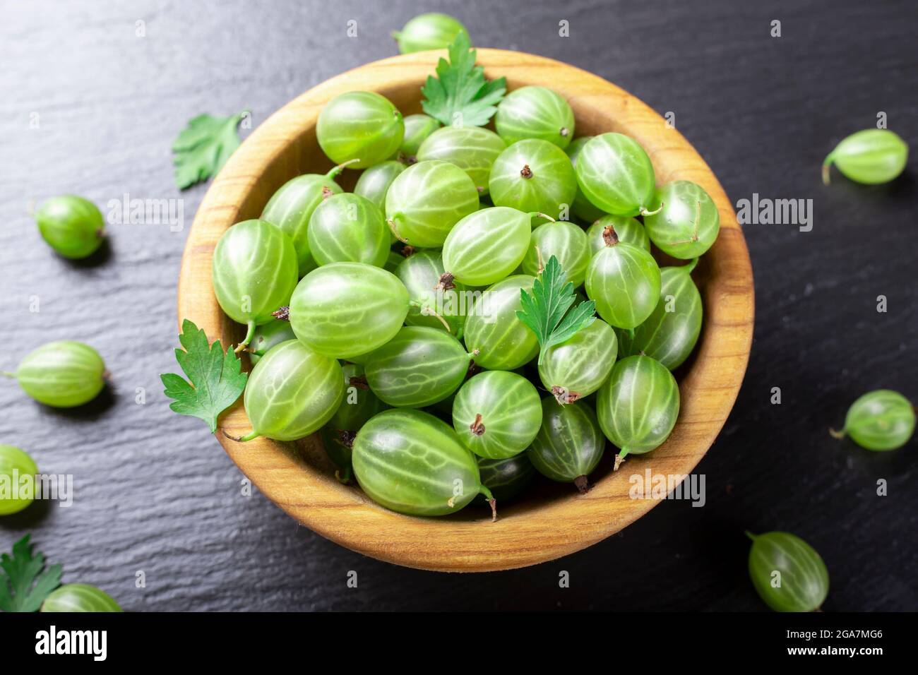 Fresh gooseberries in wooden bowl on black stone slate background. Top ...