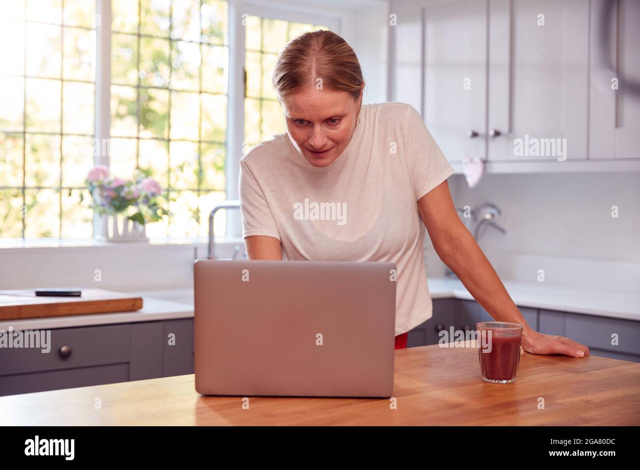 Mature Woman Wearing Fitness Clothing At Home In Kitchen Logging ...