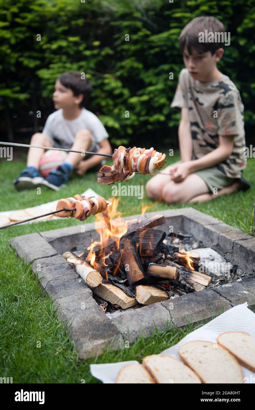 Two kids Slices of sausage, bacon and onion roasted on bonfire flame ...