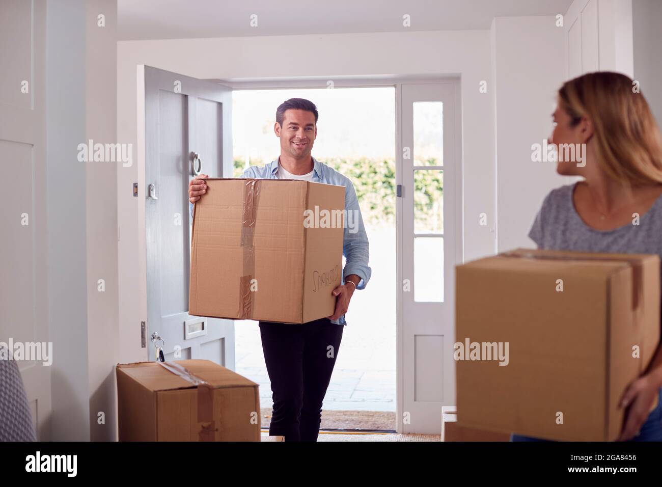 Excited Couple Carrying Boxes Through Front Door Of New Home On Moving ...
