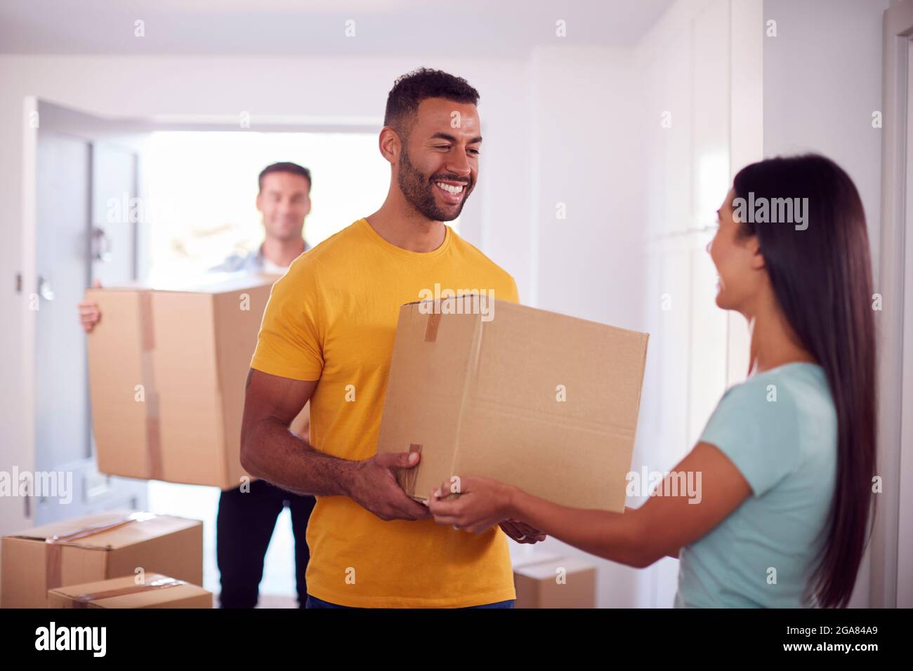 Friend Helping Couple Carry Boxes Through Front Door Of New Home On ...