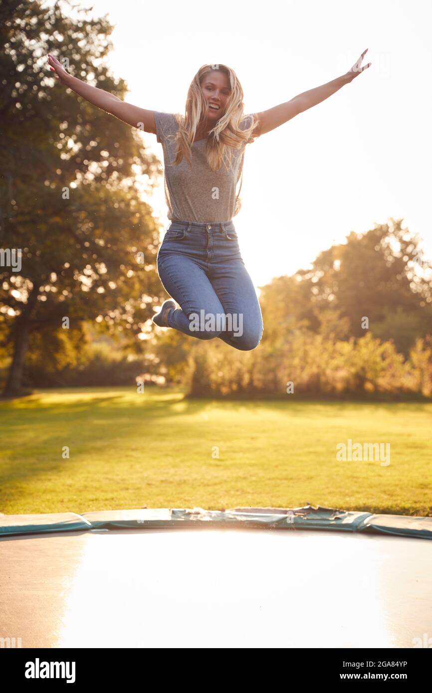 Portrait Of Woman In Mid Air Jumping On Trampoline Against Flaring Sun ...