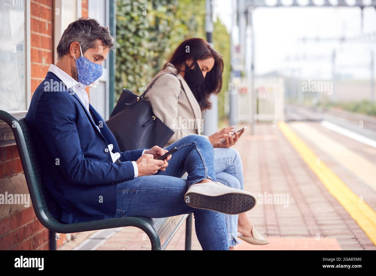 Business Commuters Sitting On Railway Platform With Mobile Phones ...