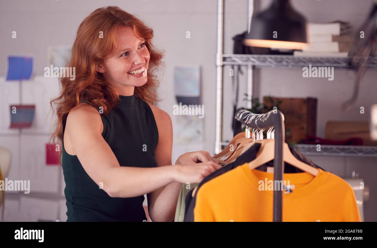 Female Owner Of Fashion Business Checking Clothing Samples On Rail In ...