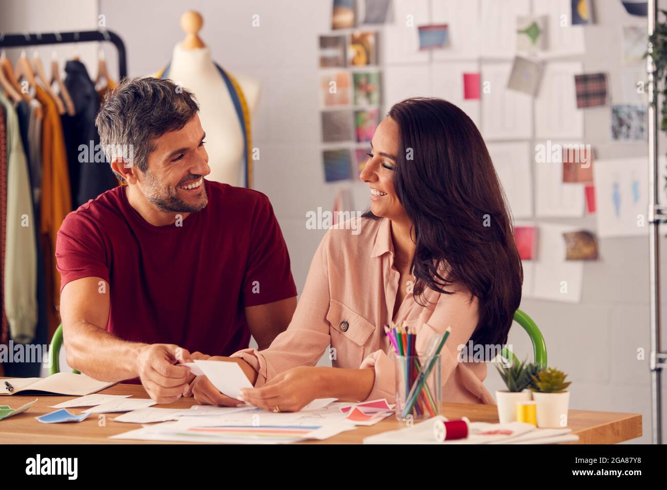 Male And Female Fashion Designers In Studio Working On Sketches And ...