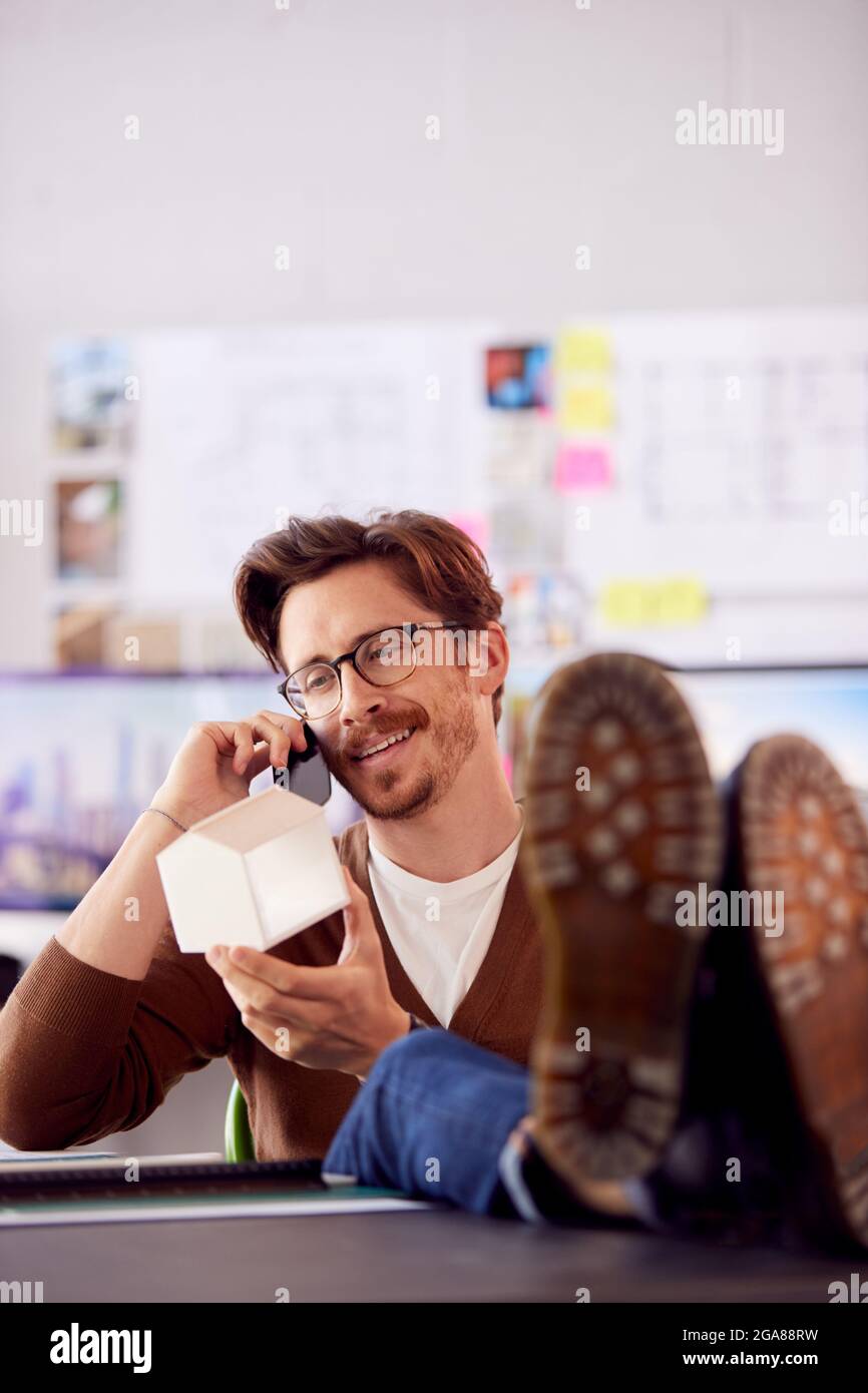 Male Architect In Office With Feet On Desk Taking Call On Mobile Phone ...