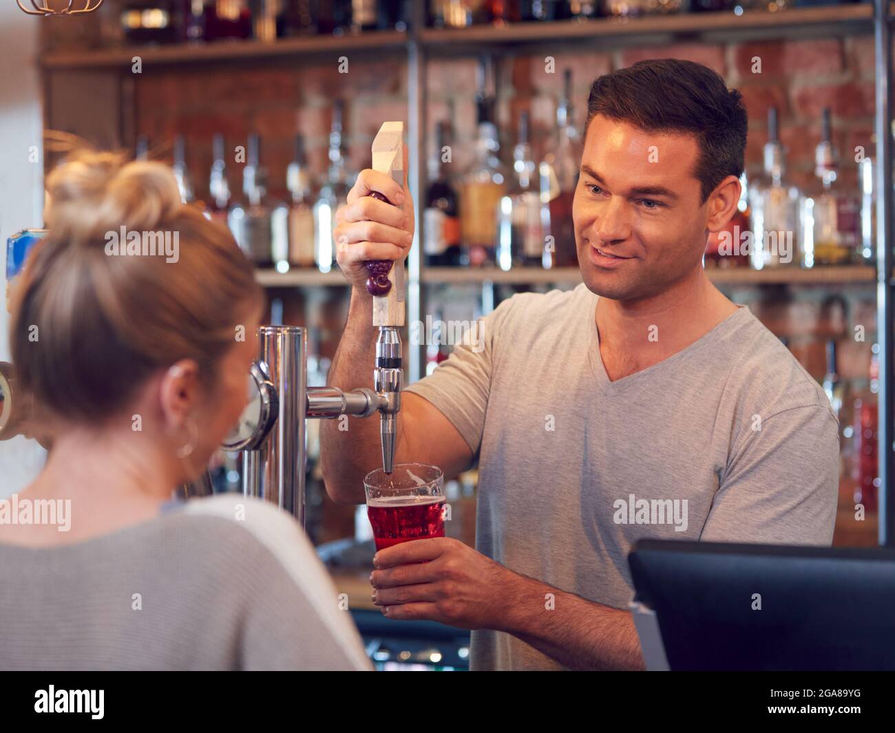 Smiling Male Bartender Behind Counter Serving Female Customer With Beer ...
