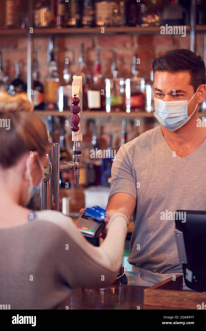 Female Customer Wearing Mask In Bar Making Contactless Payment For ...