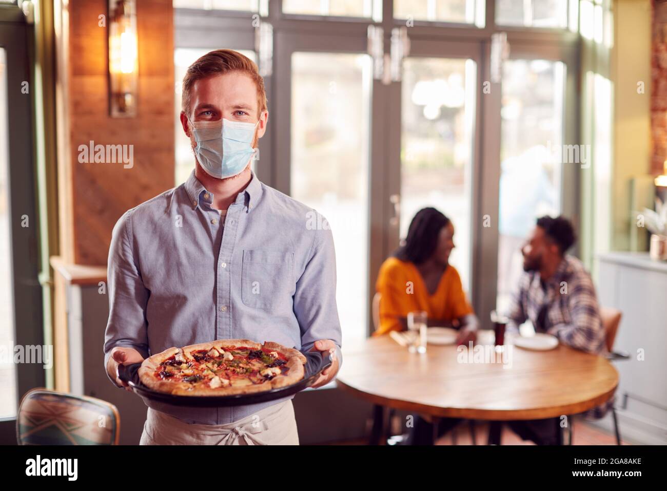 Portrait Of Waiter In Restaurant Wearing Mask Serving Pizza To Couple ...