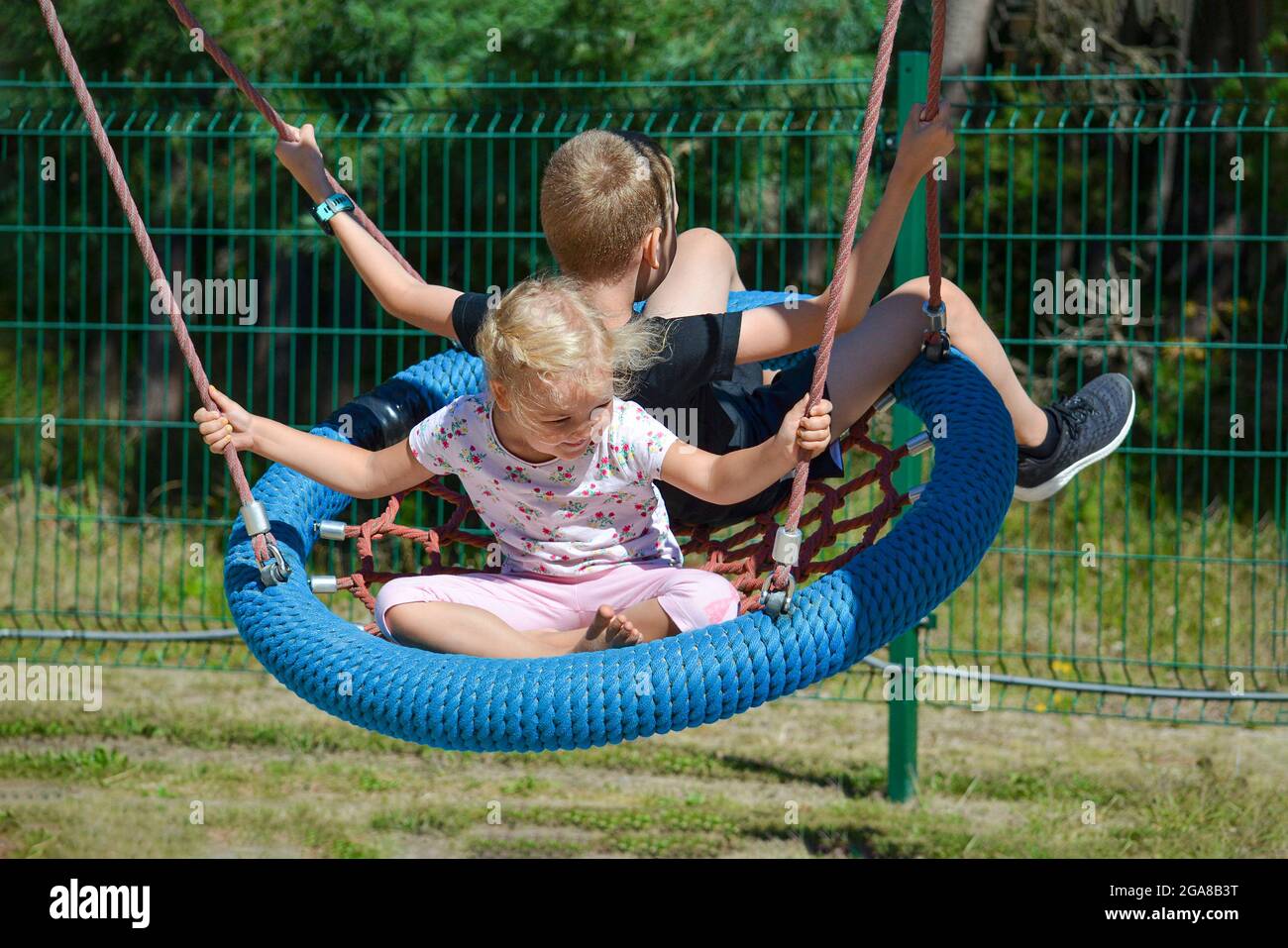 Children on a swing. Boy and girl ride a swing in the park on a summer ...