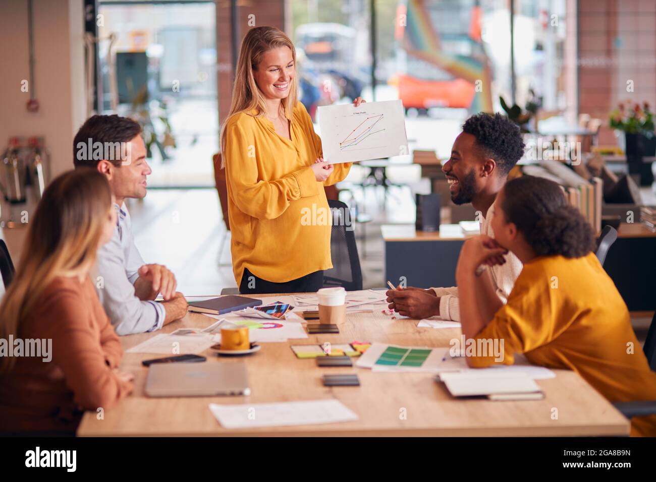 Businesswoman Giving Presentation To Colleagues Sitting Around Table In ...