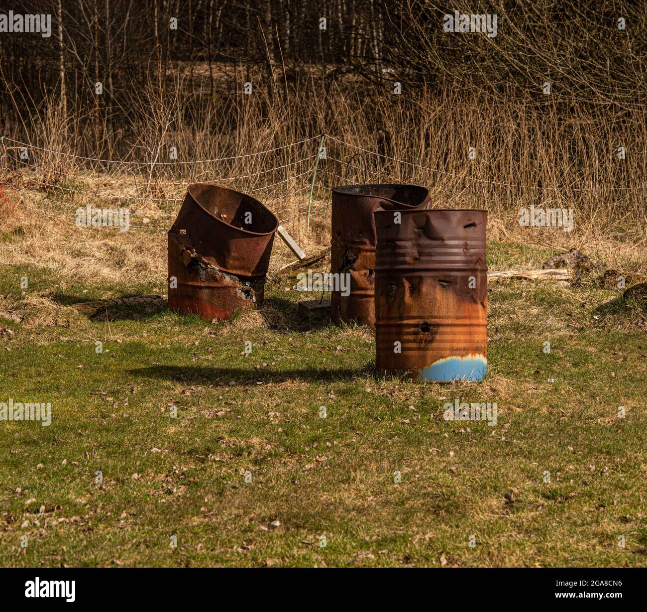Three burnt out metal barrels in a field Stock Photo - Alamy