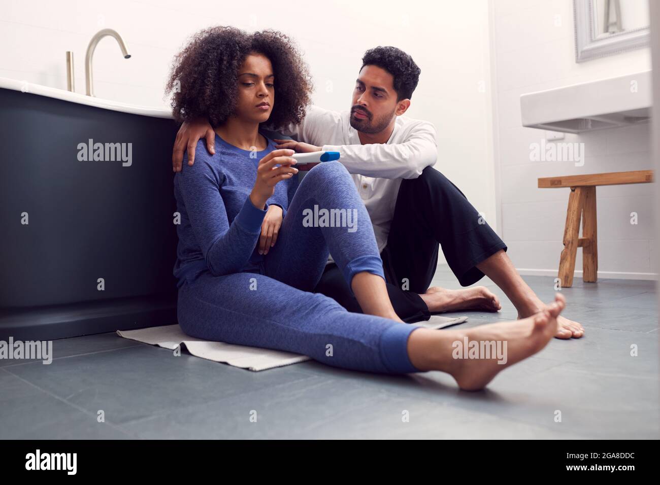 Disappointed Couple Sitting On Floor In Bathroom At Home With Negative ...