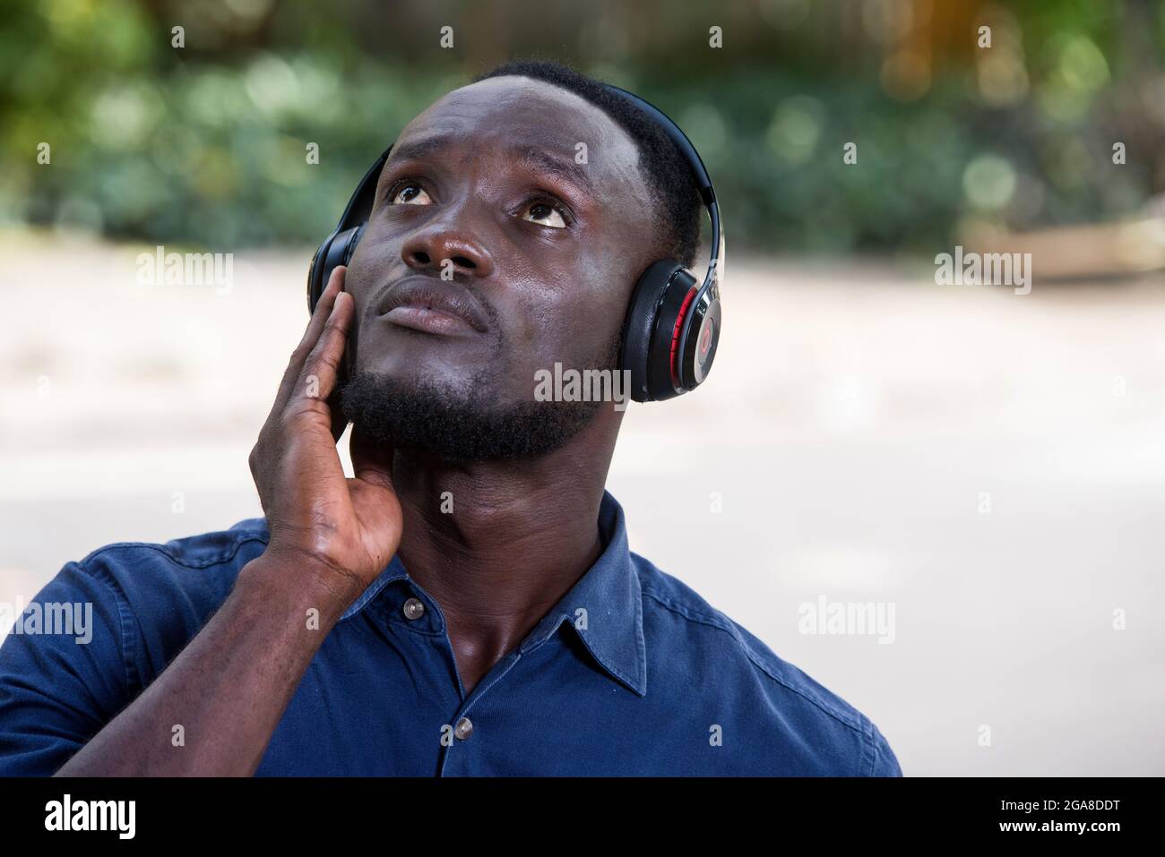 Young man standing outdoors listening to music using headphones while ...