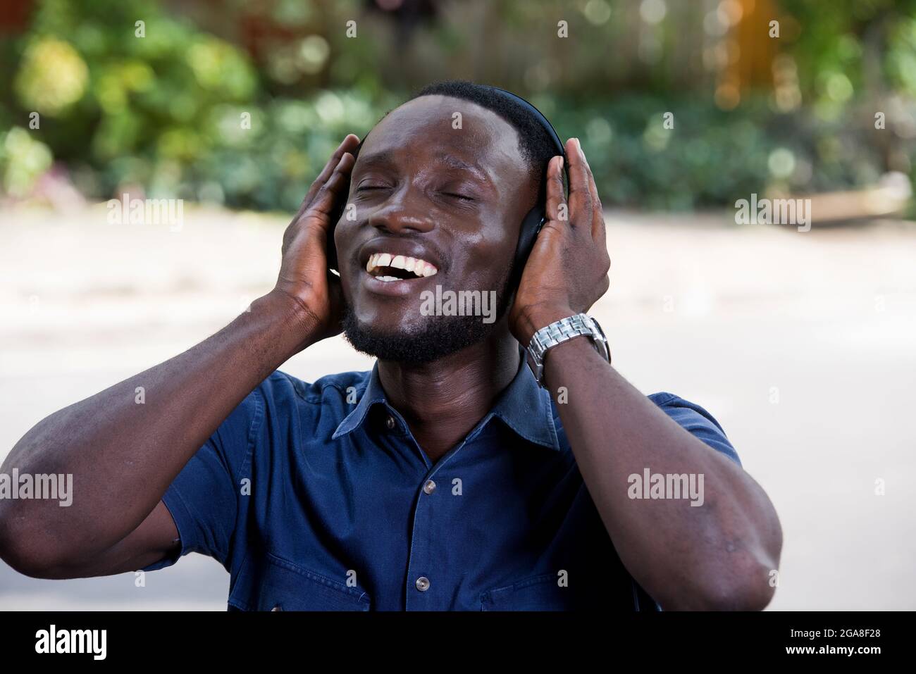 Young man standing outdoors listening to music using headphones while ...