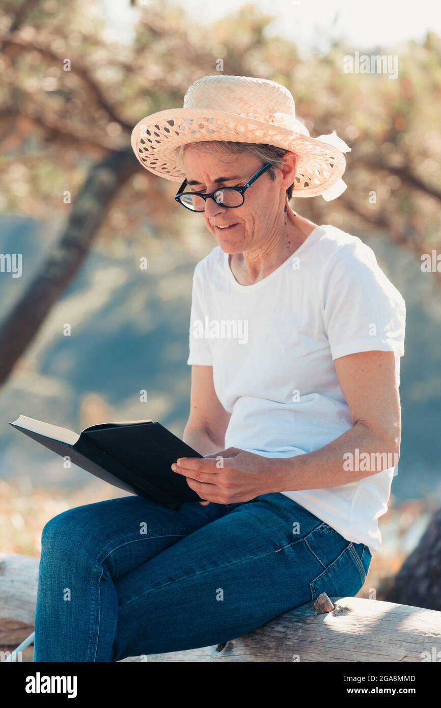 Elderly beautiful woman from Spain with a straw hat reading a book on a ...