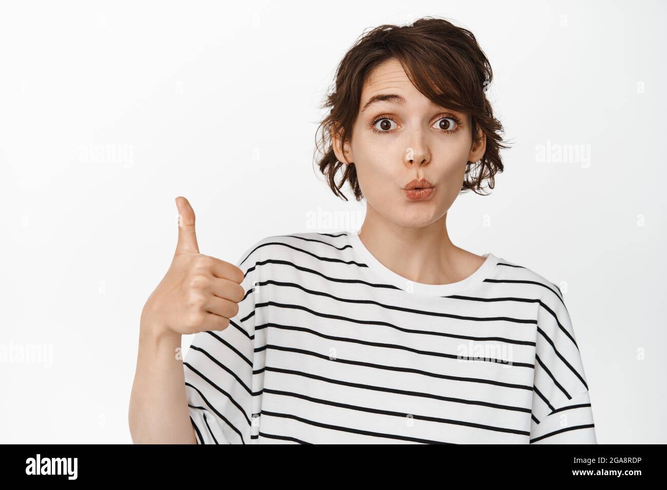 Surprised brunette woman shows thumbs up and look excited, like ...