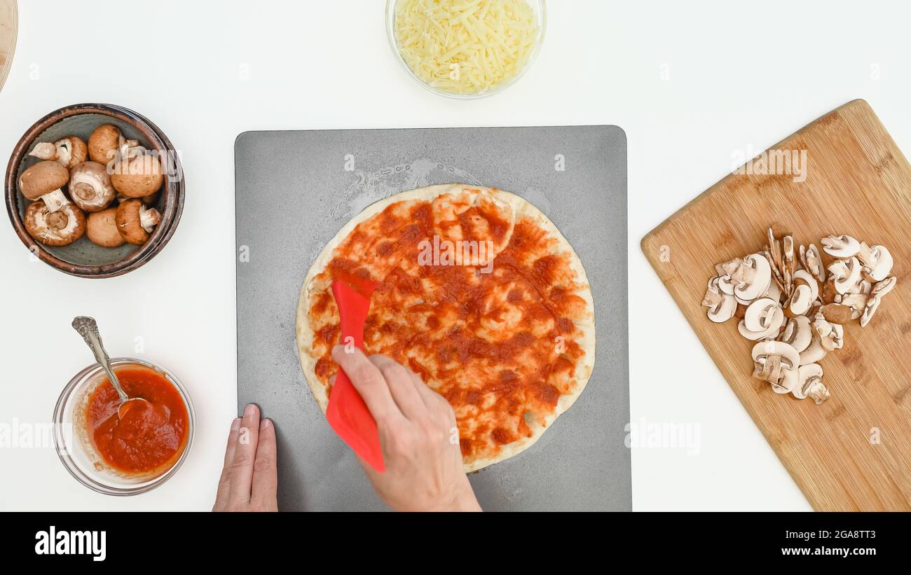Topping pizza dough with tomato sauce, close up preparation process ...