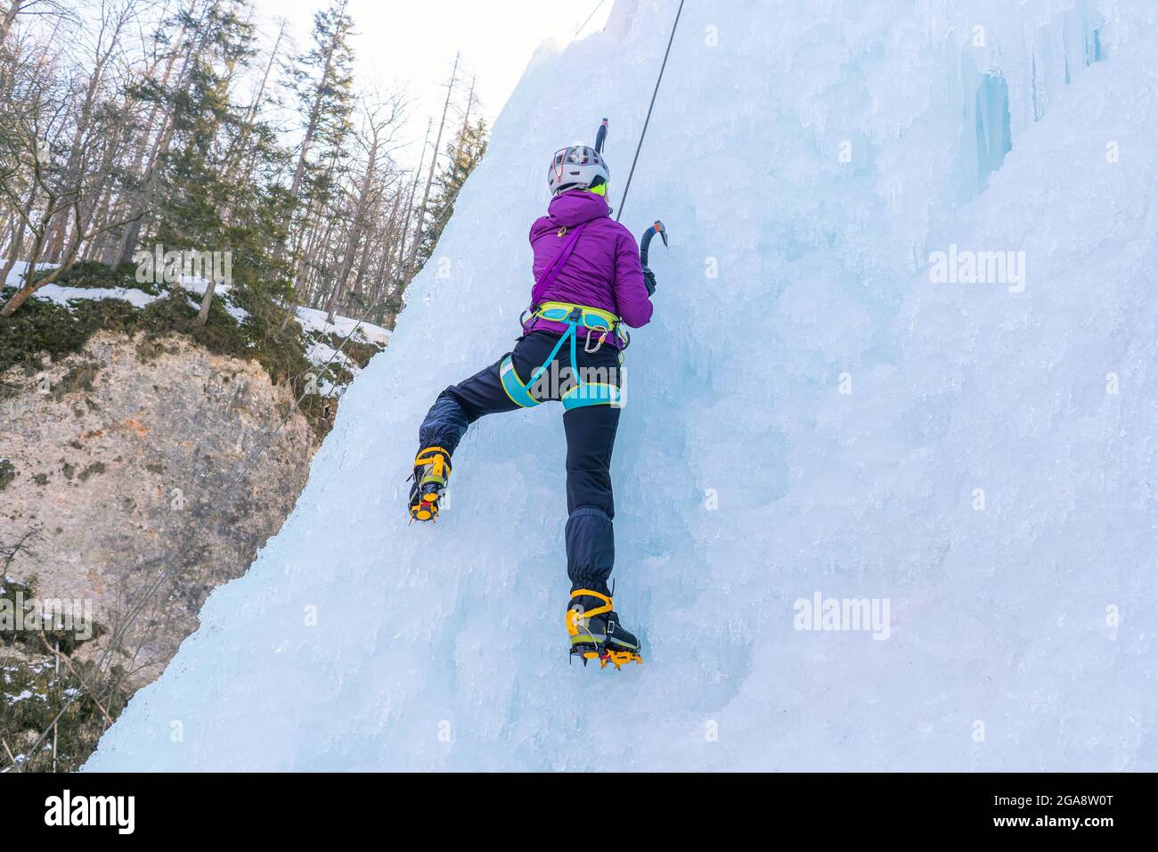 Female ice climber in traction position, swinging ice axes overhead and ...