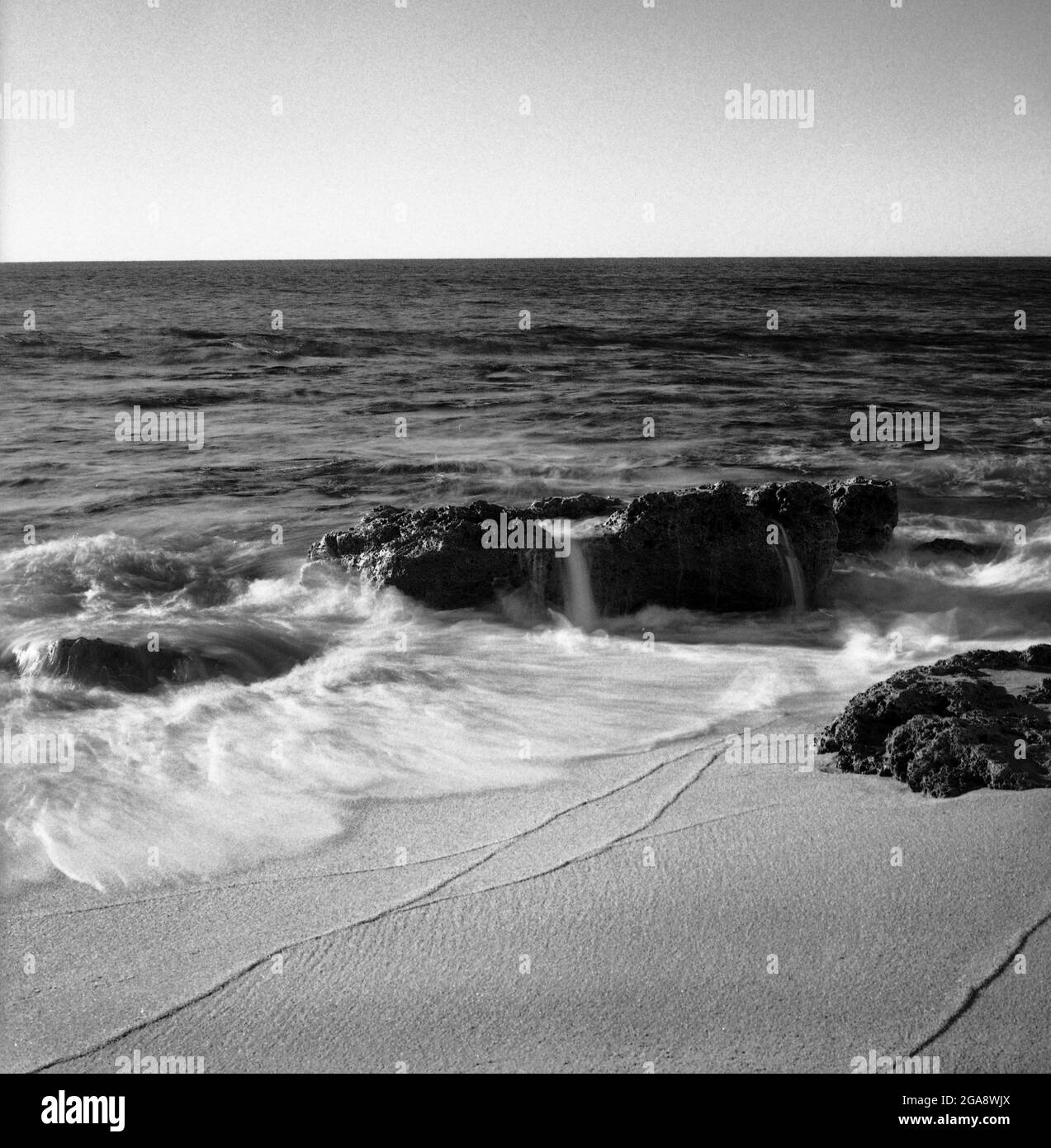 Black and white shot of sea waves crashing on the rocks on the beach ...