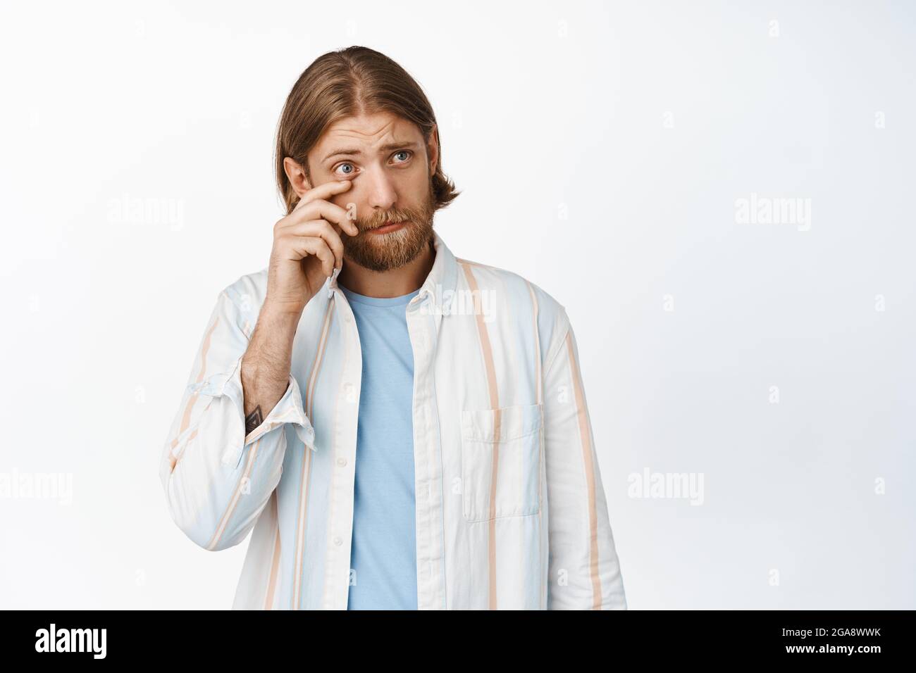 Young blond man sympathizing, crying, wiping tear below eye and looking ...