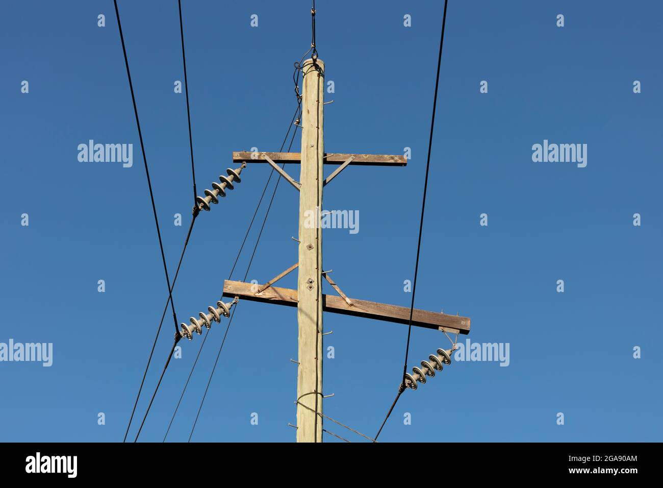 Photograph of a wooden telephone post and cables against a blue sky ...