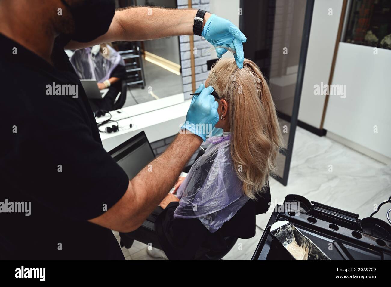 Business woman working on laptop while hairdresser stylist coloring a ...