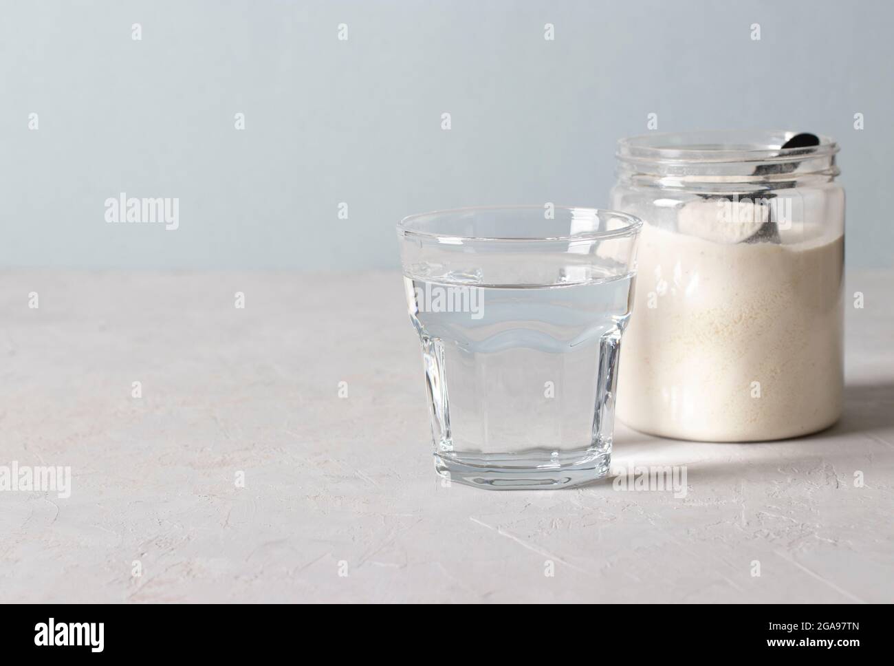 Glass of water, Collagen powder in jar with measuring spoon on a light ...