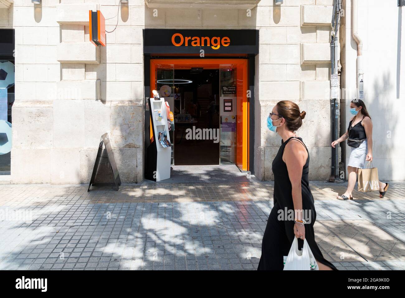Two women walking by an Orange mobile store in Valencia Stock Photo - Alamy