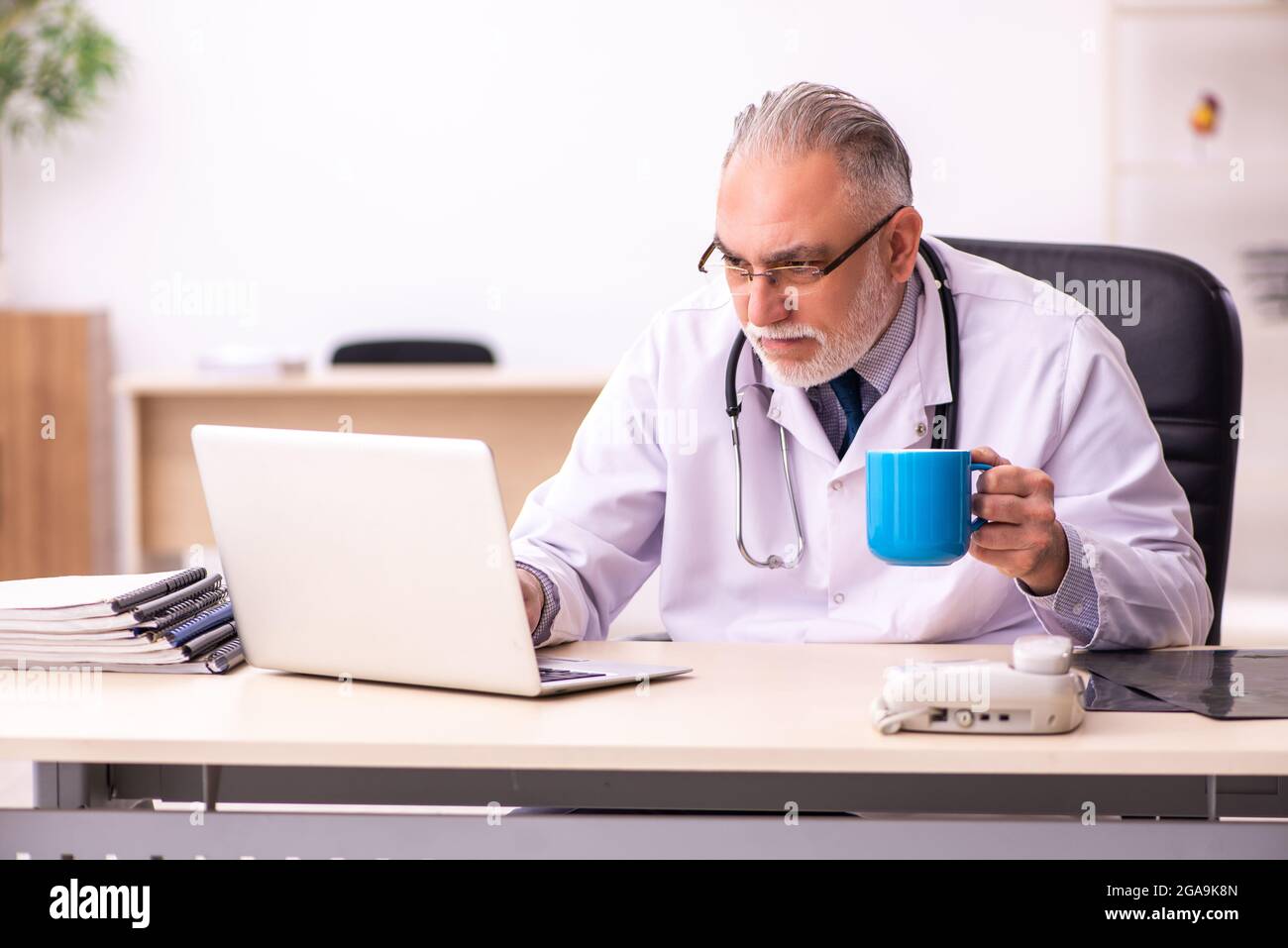 Aged male doctor drinking coffee at workplace Stock Photo - Alamy