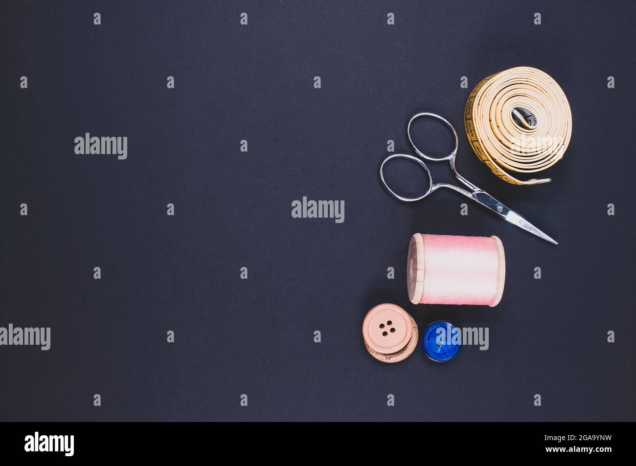 Flat lay of scissors, measuring tape, buttons, and thread on a dark ...