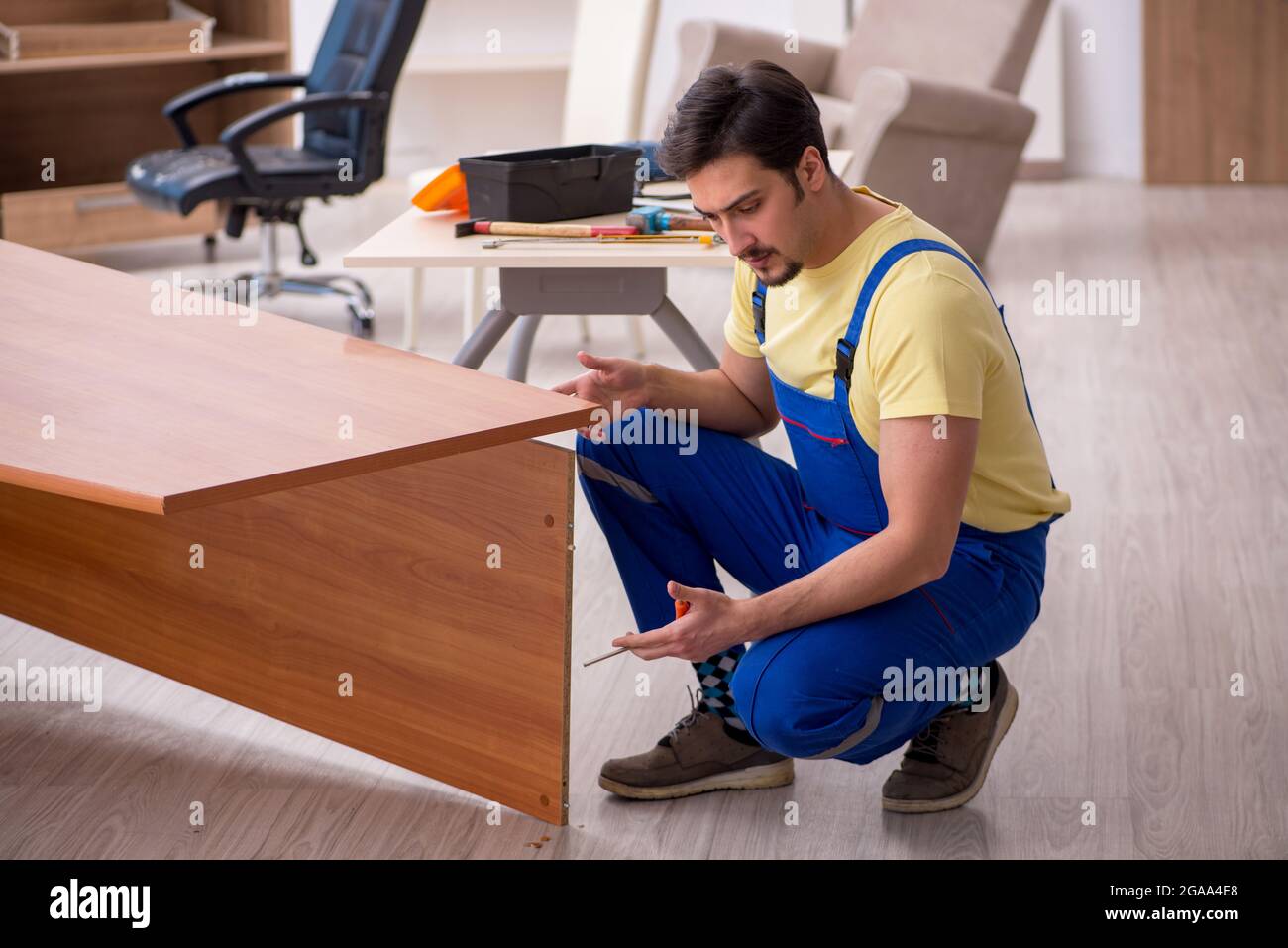 Young carpenter repairing desk in the office Stock Photo - Alamy