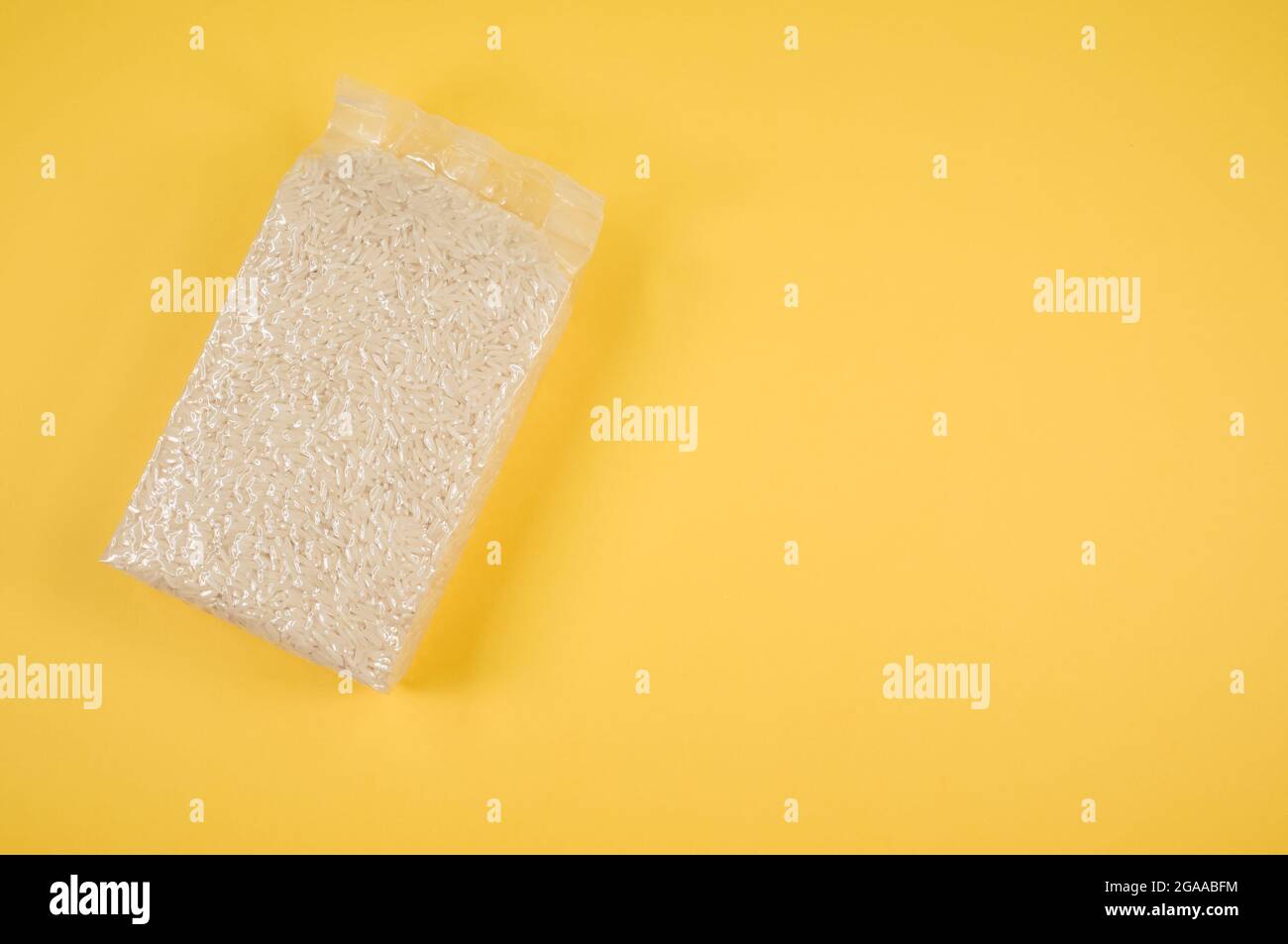 Pack of rice grains isolated on a yellow background with free space for ...
