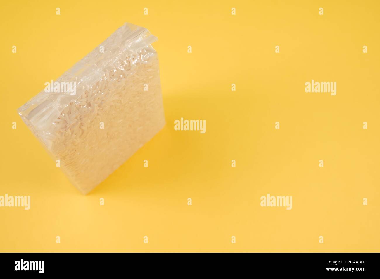 Pack of rice grains isolated on a yellow background with free space for ...