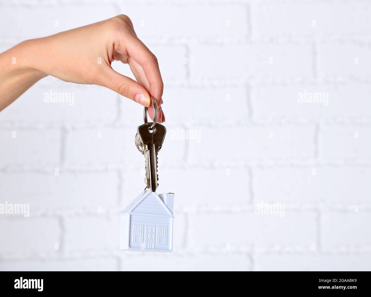 Female hand holding keys with house key chain on white brick wall ...