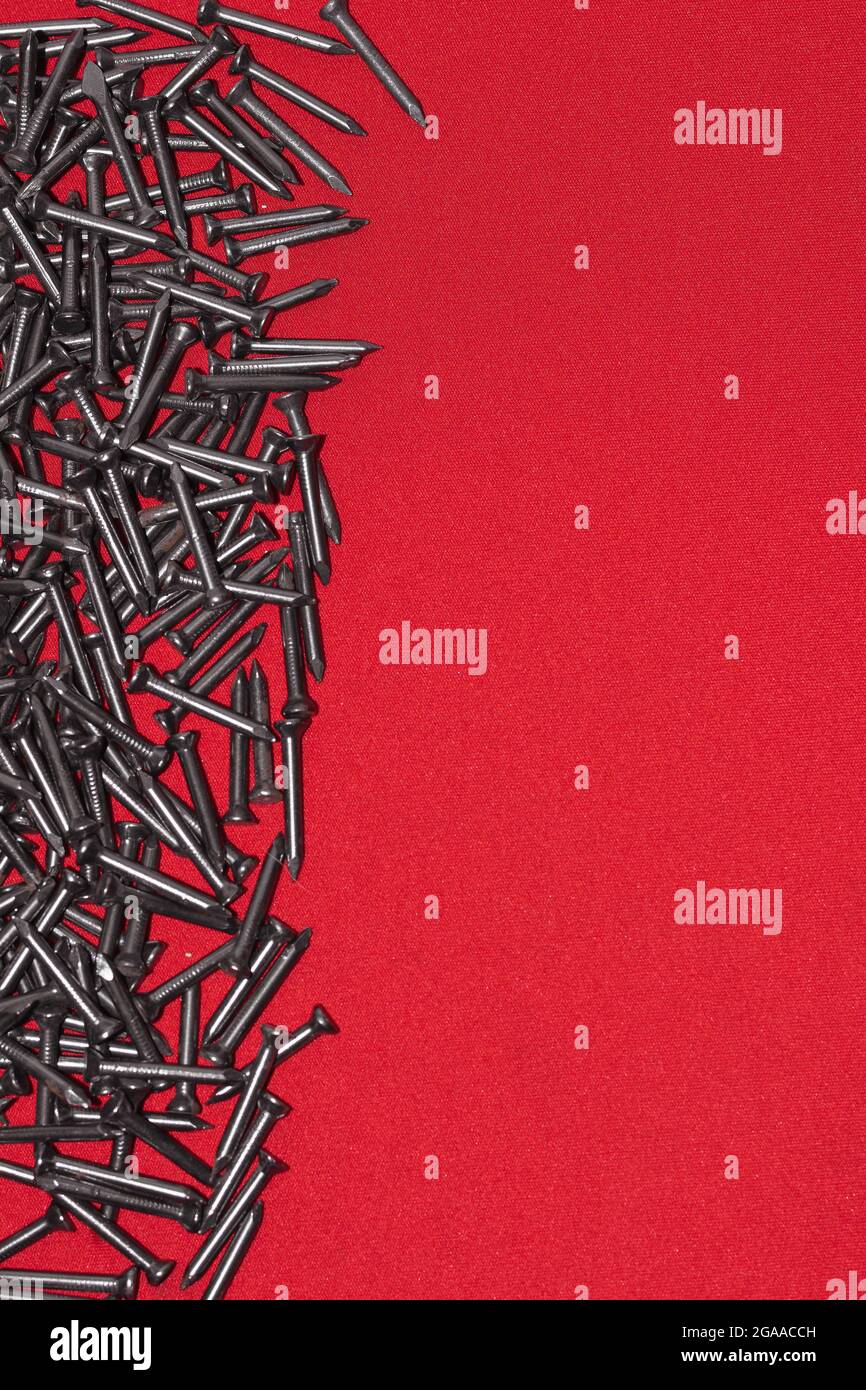 Black steel nails on red background, scattered to the left randomly ...