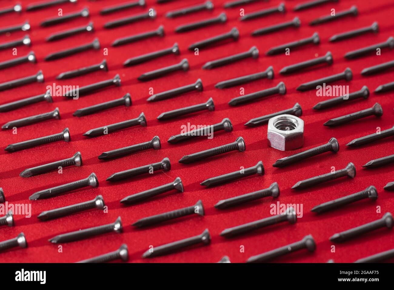 Black steel nails and nut on red background, arranged horizontally ...