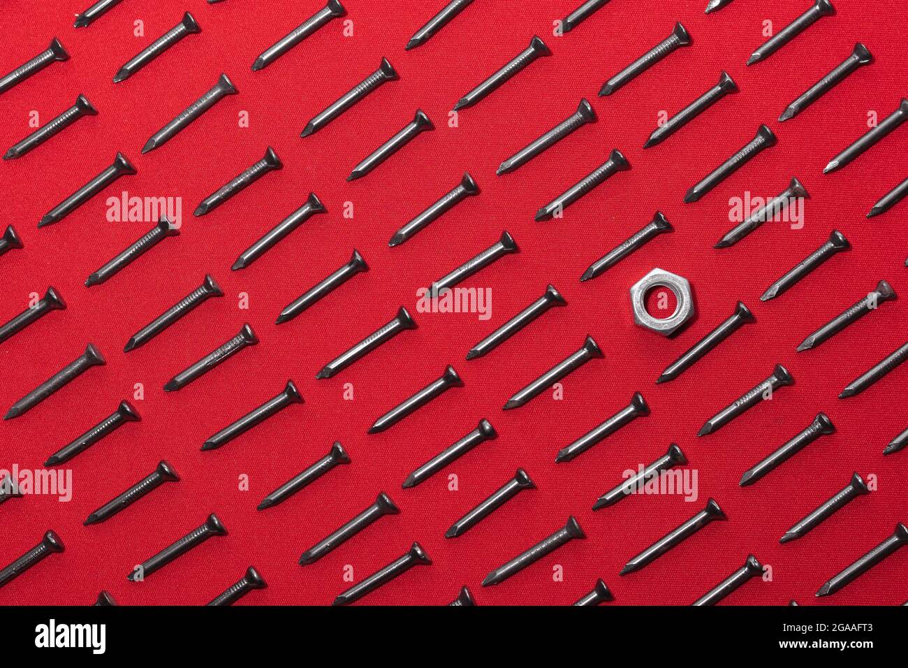 Black steel nails and nut on red background, arranged horizontally ...