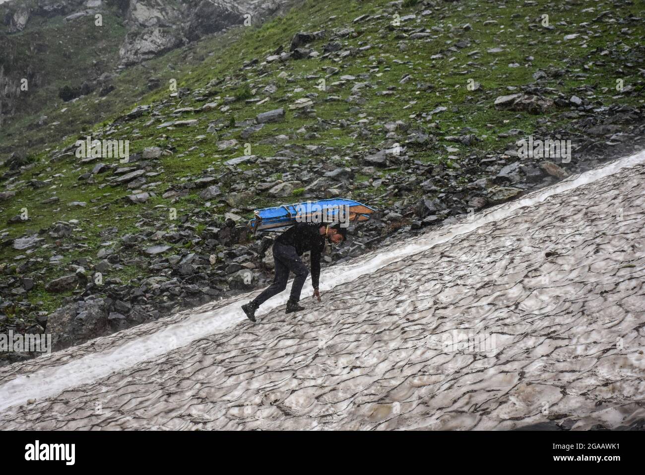 A man carries a sledge as he walks on a glacier to reach the top of the ...