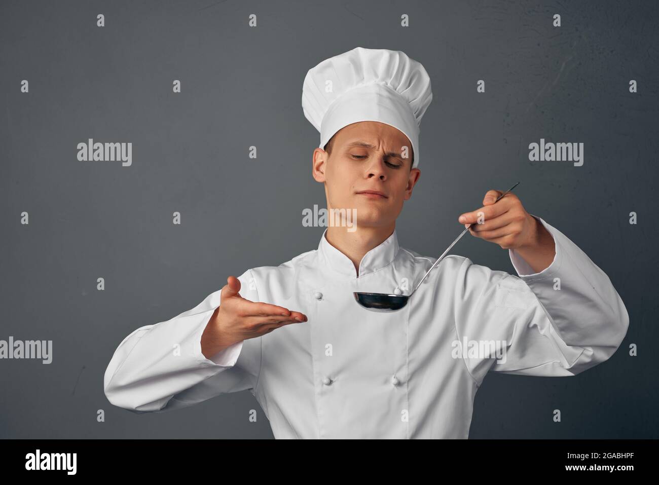 man chef's uniform with a ladle in his hands trying the dishes Stock ...