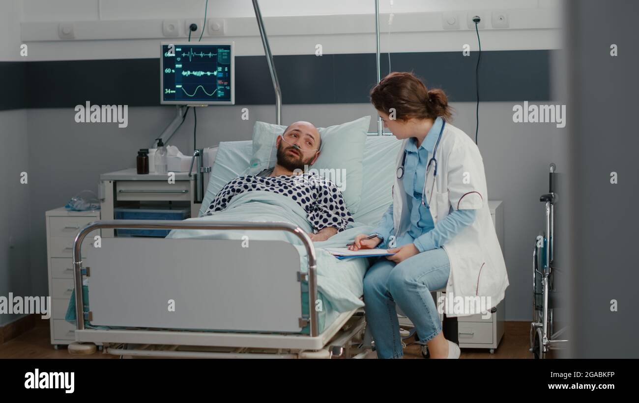 Sick man resting in bed with oxygen tube talking with doctor explaining ...