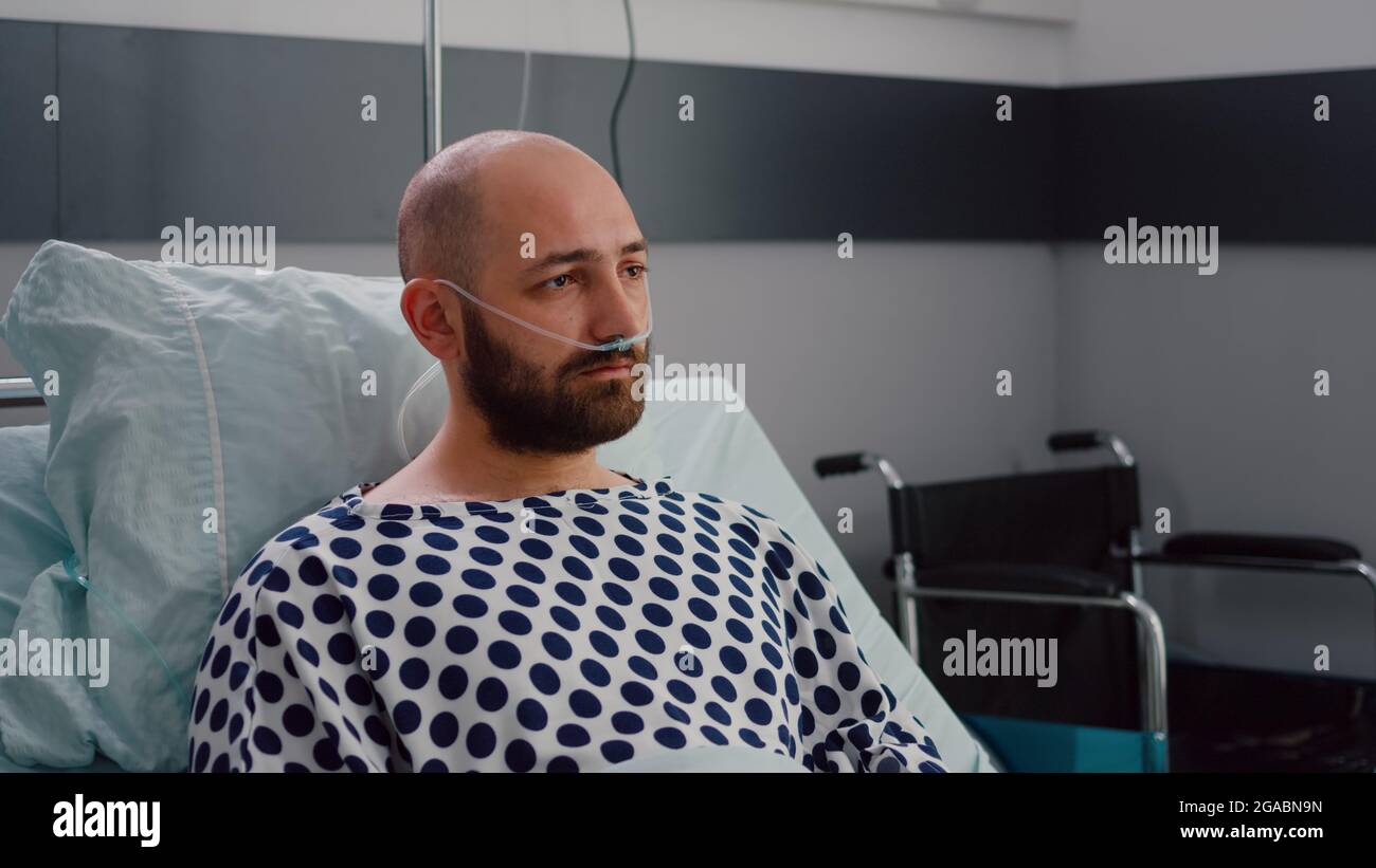 Sad sick man with nasal oxygen tube resting in bad looking into camera ...