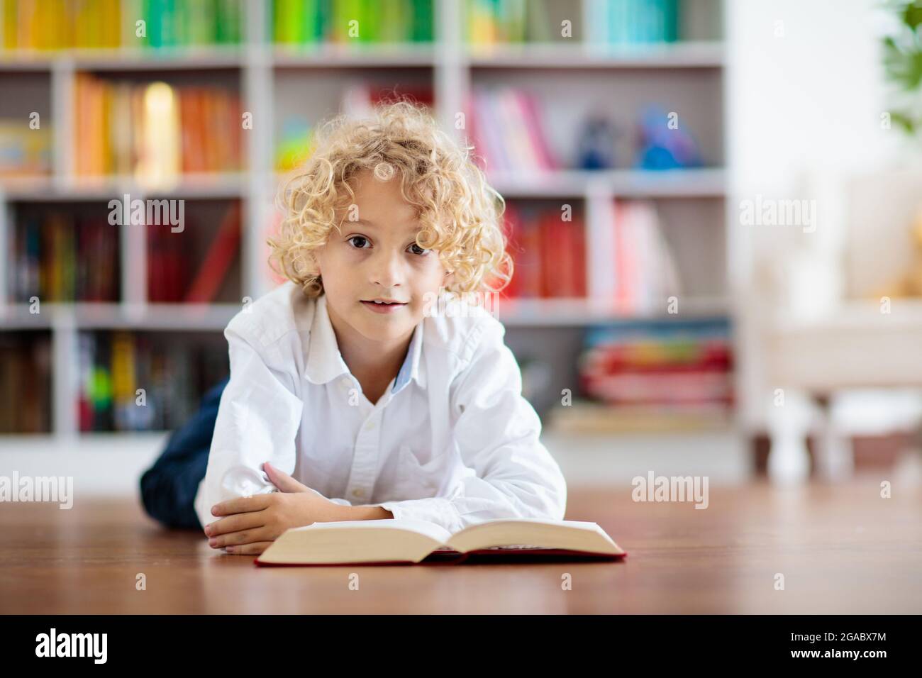 Child reading book. Kids read. Little boy at a colorful bookshelf doing ...